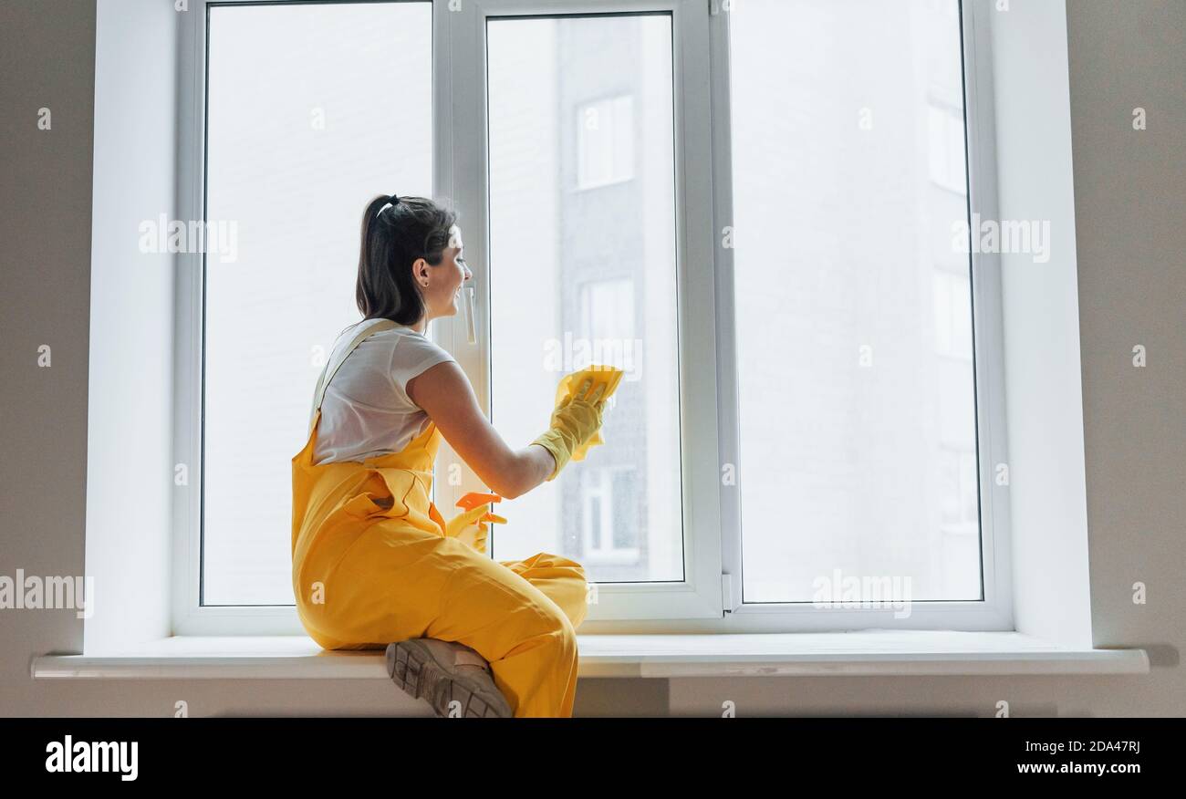 Housewife in yellow uniform cleaning windows. House renovation ...
