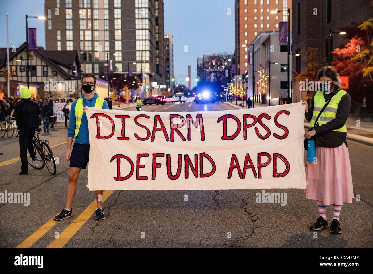 Two demonstrators hold a banner that says, "Dissarm DPSS Defund AAPD ...