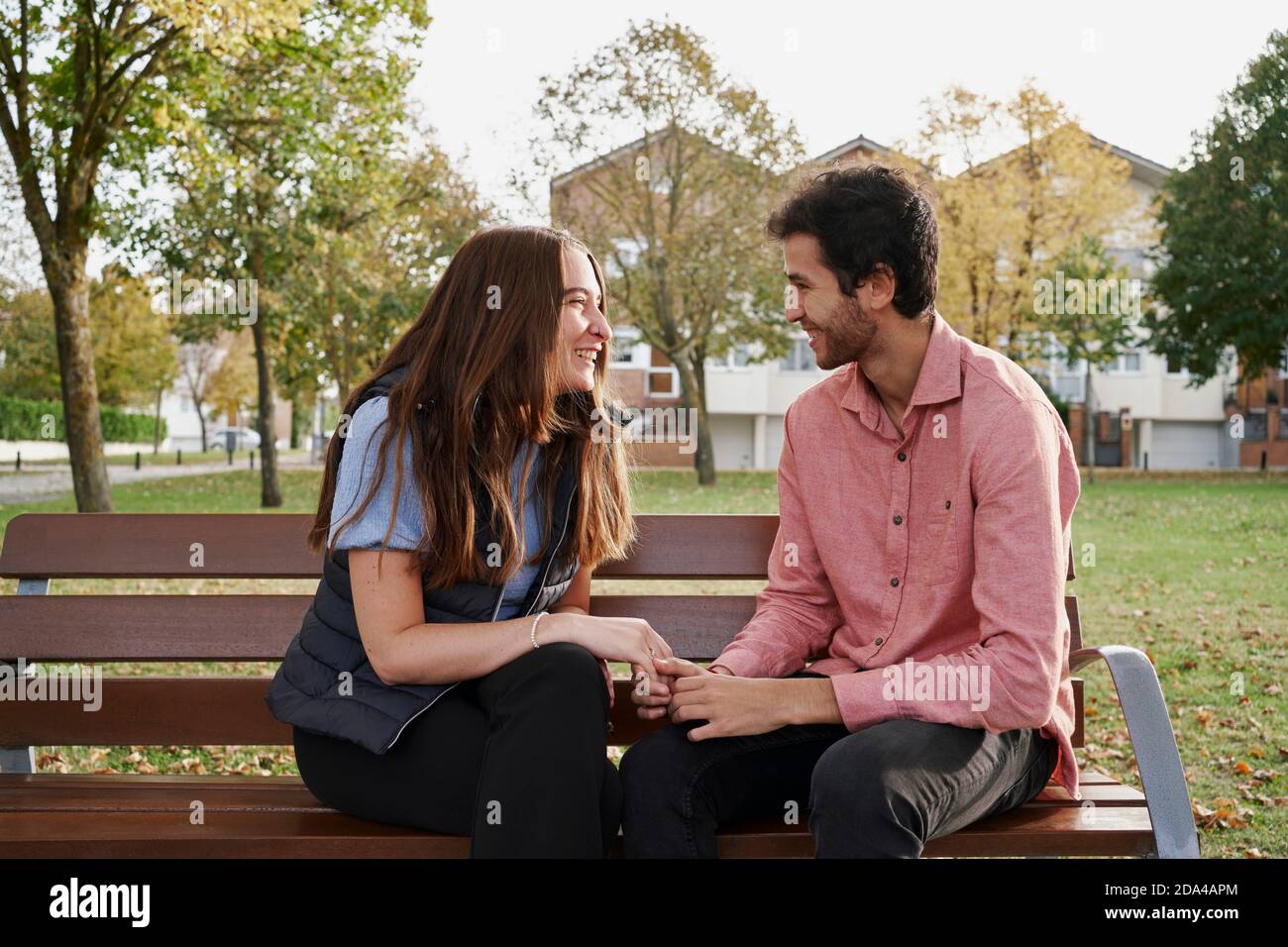 Young couple smiling and staring at each other sitting on the bench in ...