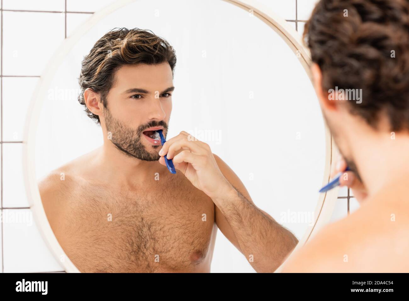 Shirtless man brushing teeth while looking at mirror in bathroom Stock ...
