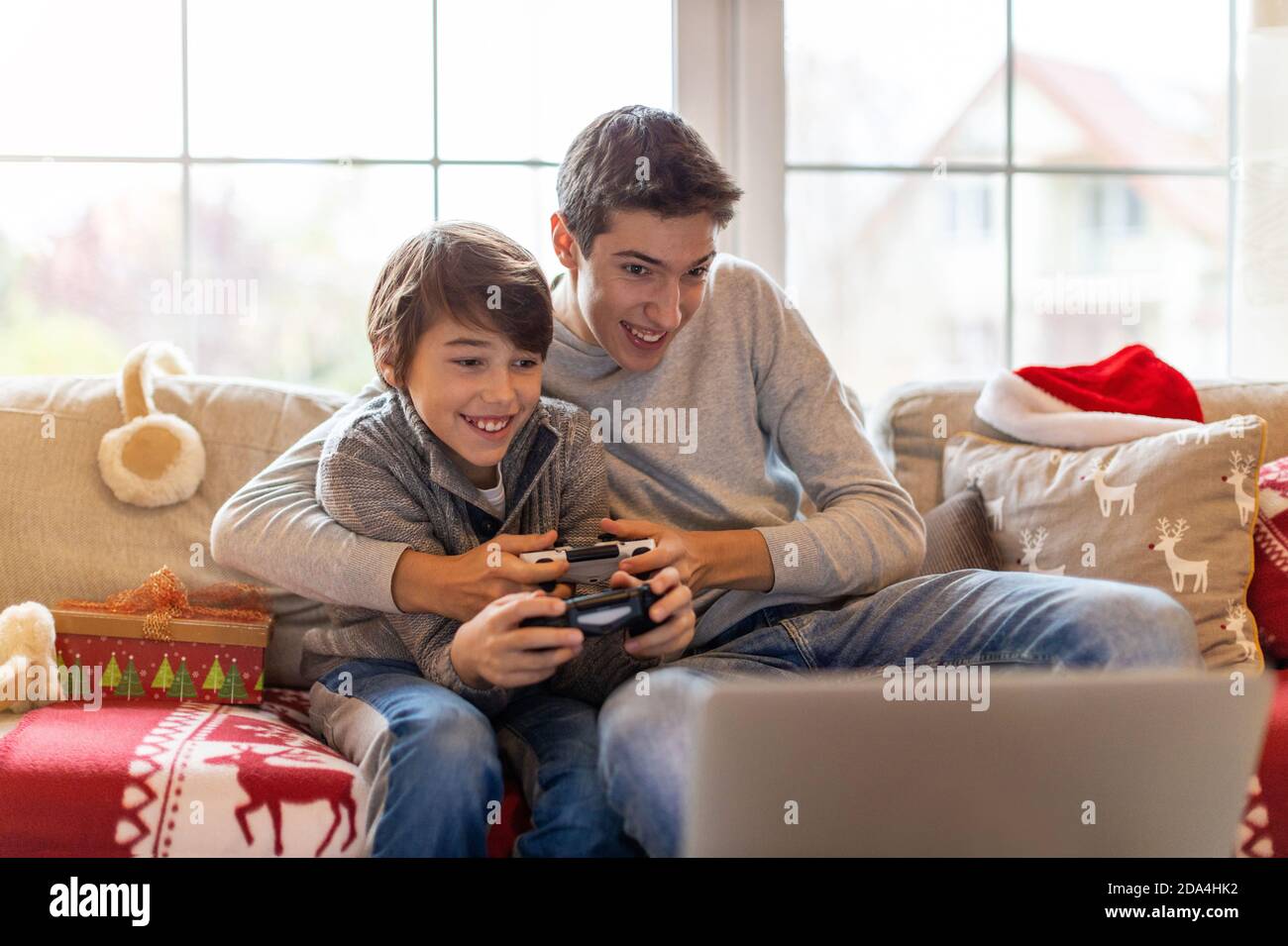 Two young brothers sitting on the couch at home, smiling while playing ...
