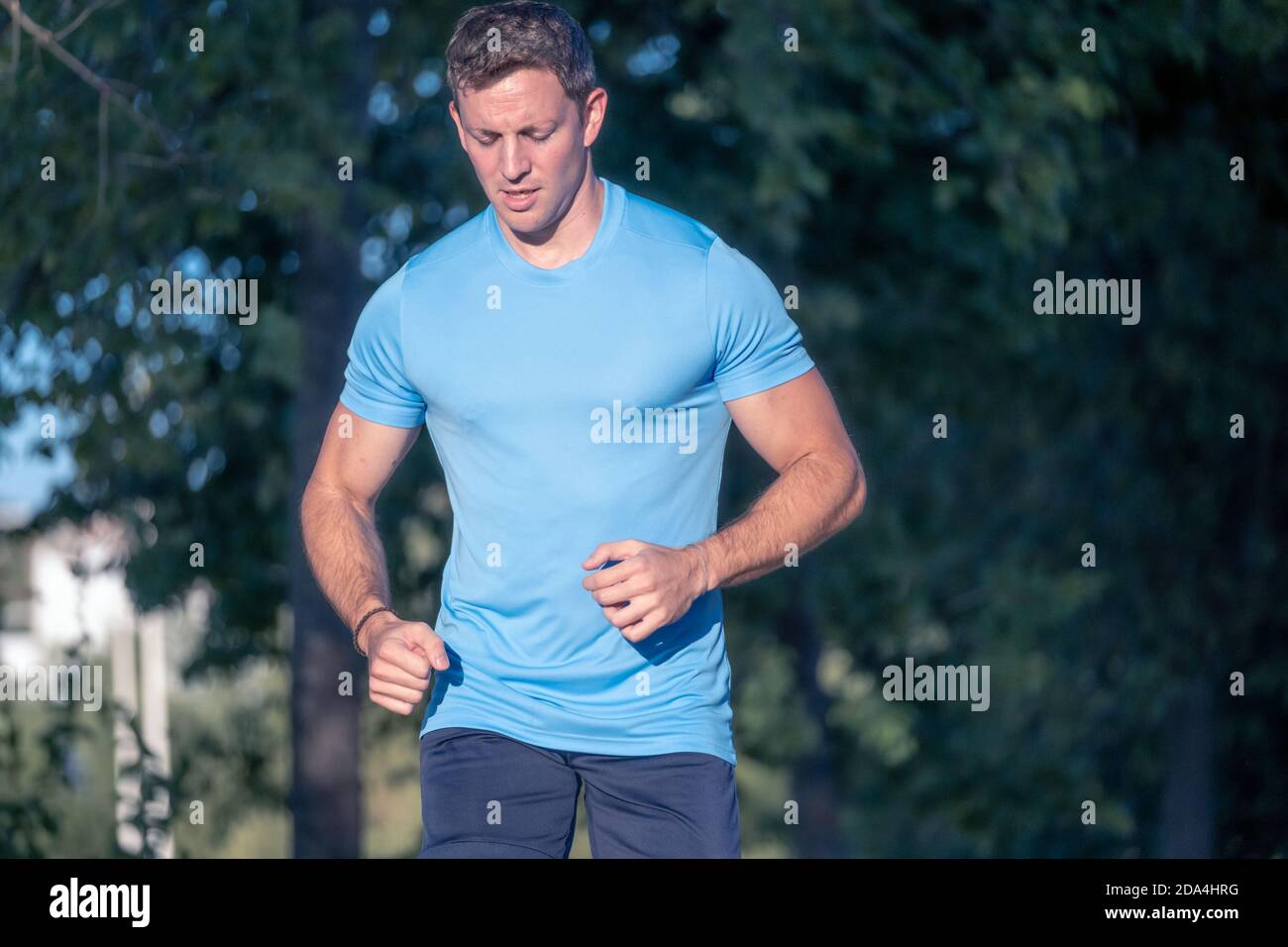 Young man wearing a blue shirt running in a park with trees in the ...