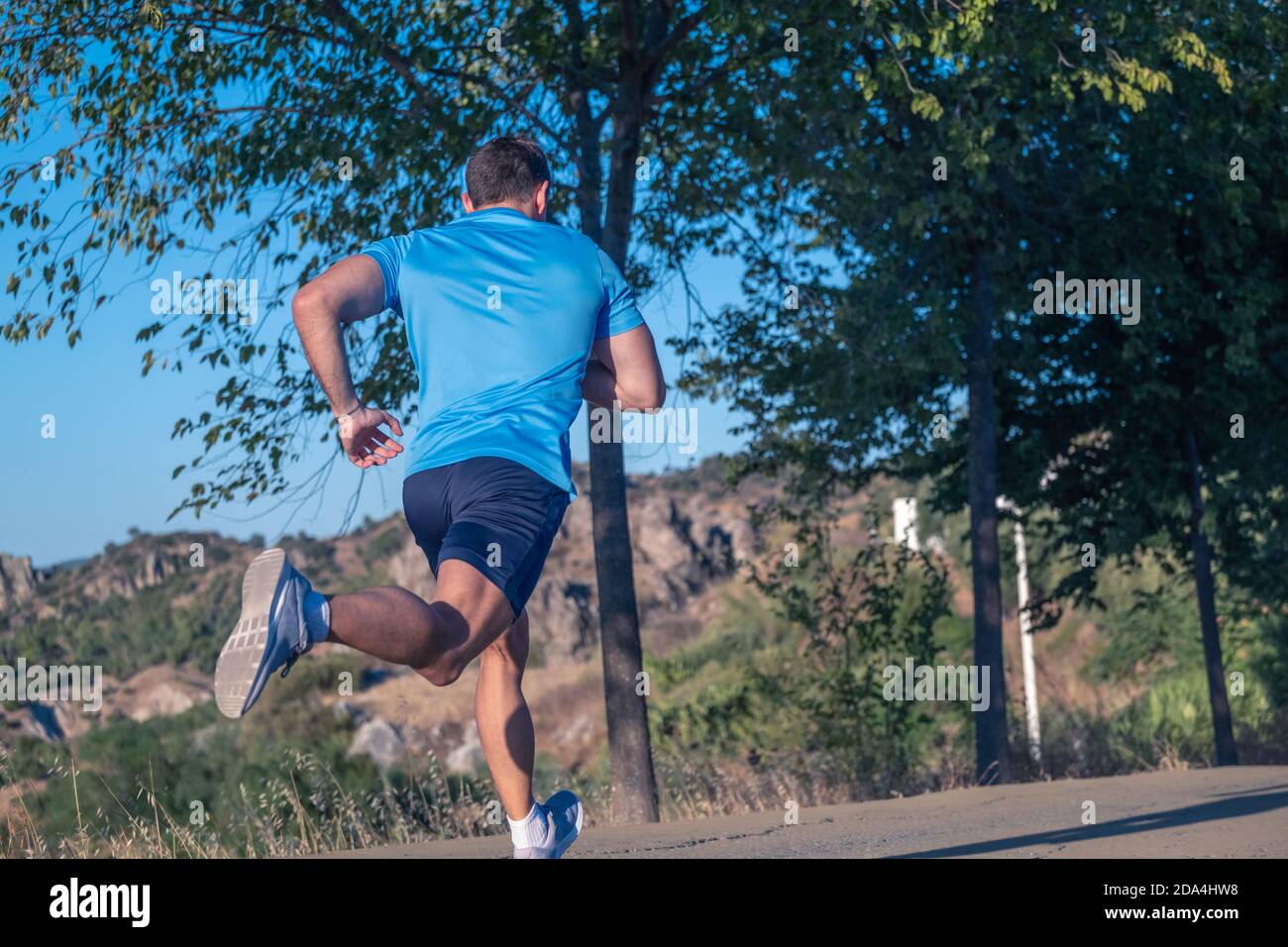 Young man wearing a blue shirt running in a park with trees in the ...