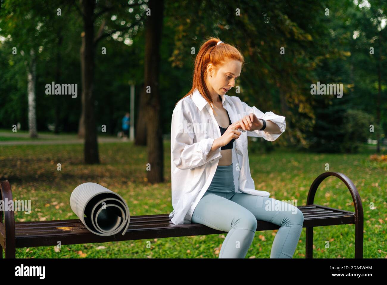 Medium shot of beautiful red-haired young woman sitting on a bench in ...