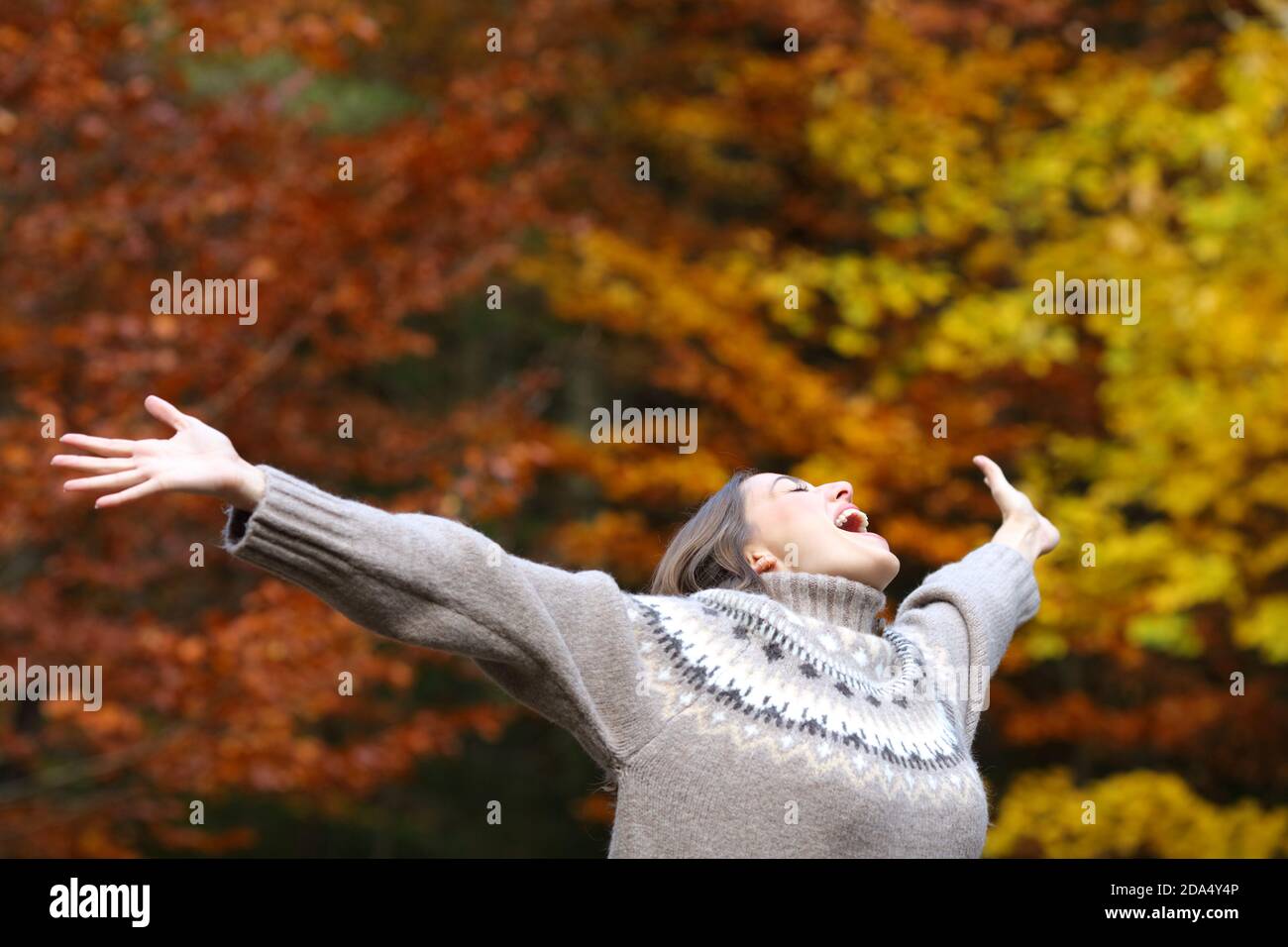 Excited woman celebrating autumn stretching arms in a beautiful forest ...