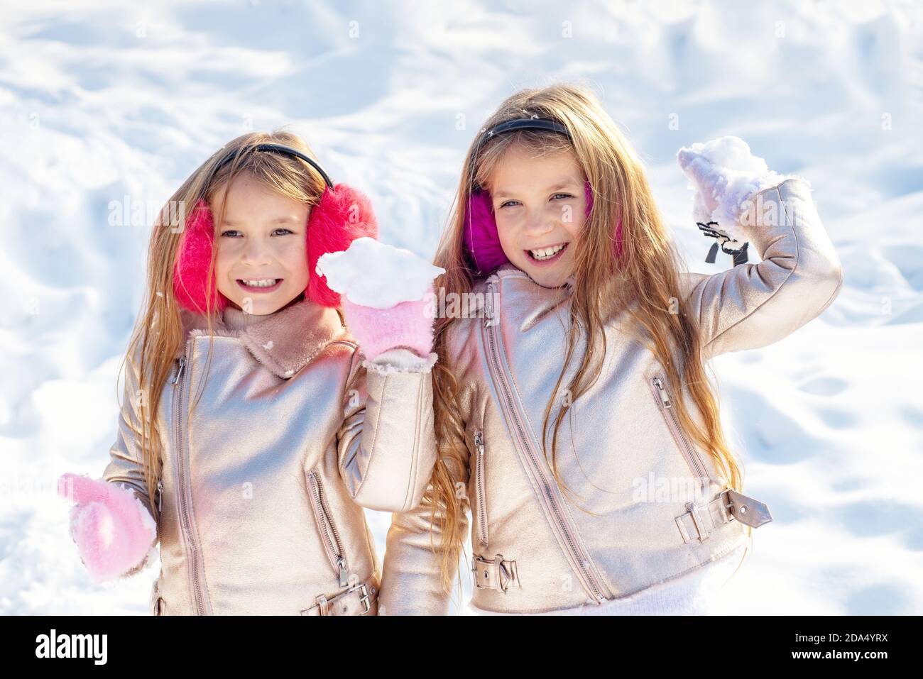 Little girls throw snowball in park. Portrait of two little girls play ...