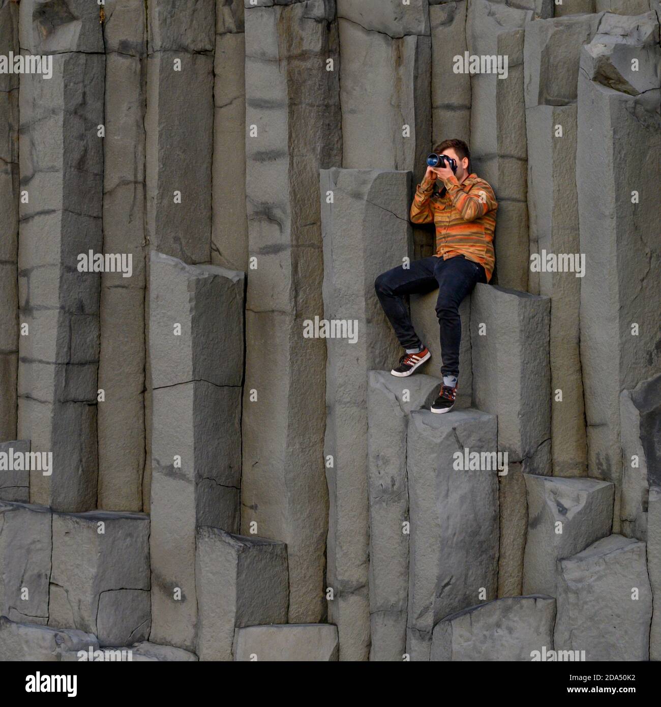 Man sitting on basalt rock taking picture with camera, Reynisfjara ...