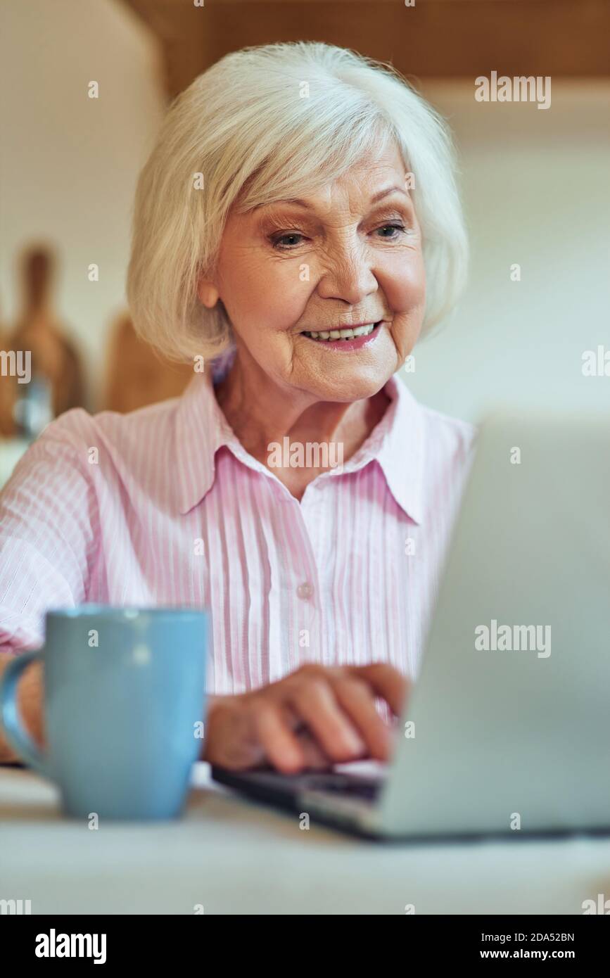 Close up of smiling beautiful elderly woman using laptop and typing ...