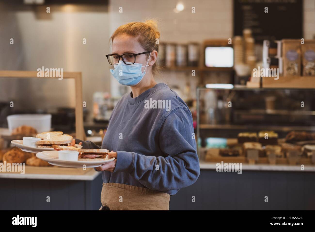 Blond waitress wearing face mask working in a cafe, carrying plates of ...