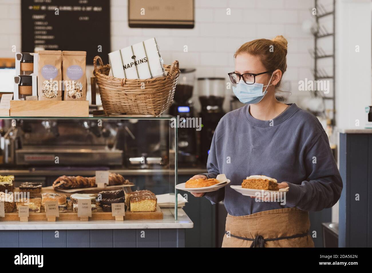 Blond waitress wearing face mask working in a cafe, carrying plates of ...
