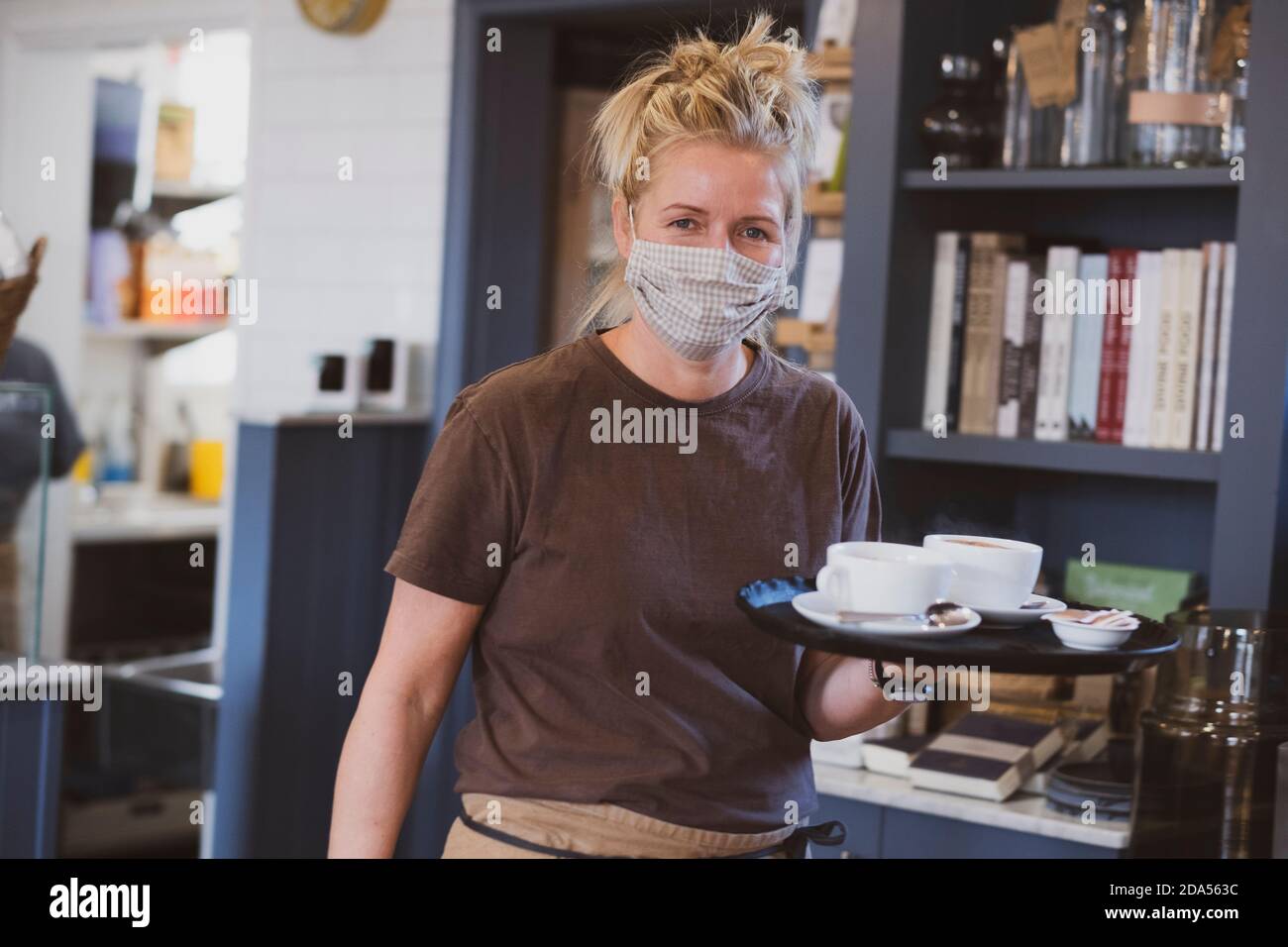 Blond waitress wearing face mask working in a cafe, carrying tray with ...