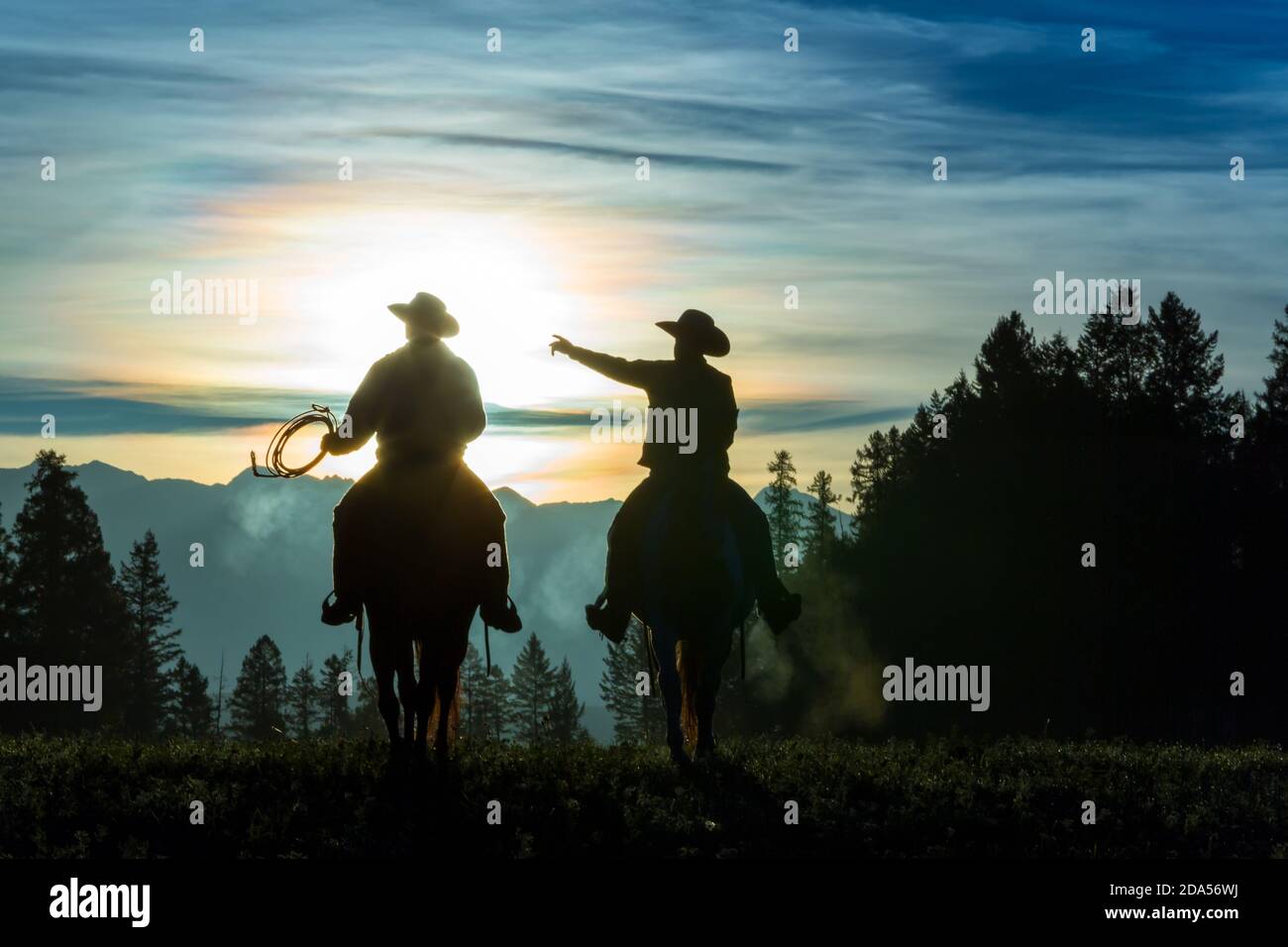 Two cowboys riding across grassland with mountains in background, early ...