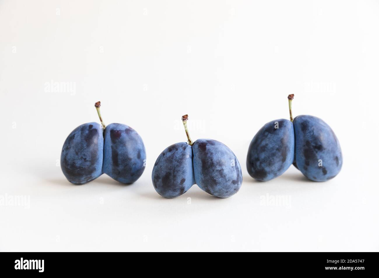 Ugly organic blue double plums heart-shaped on a white background. The ...