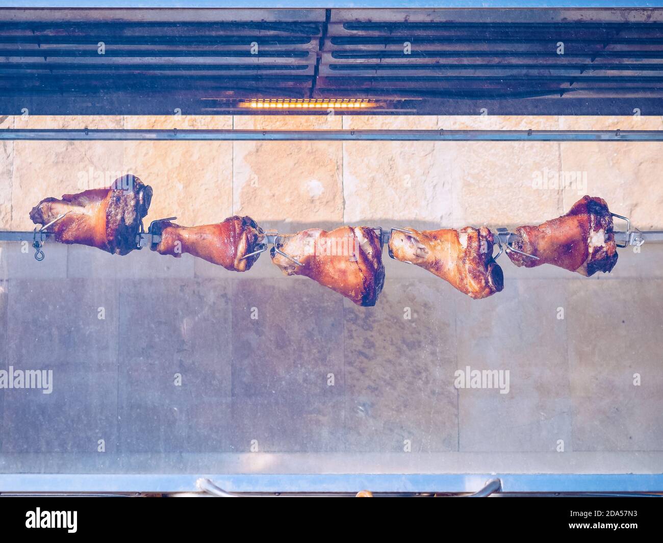 Golden pork legs are fried on a spit behind glass outside Stock Photo ...