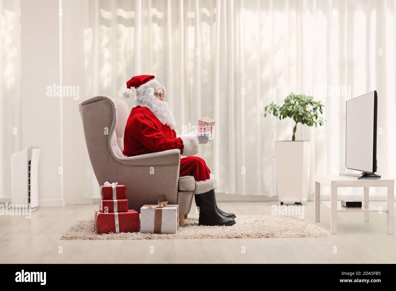 Full length profile shot of santa claus in armchair eating popcorn and ...