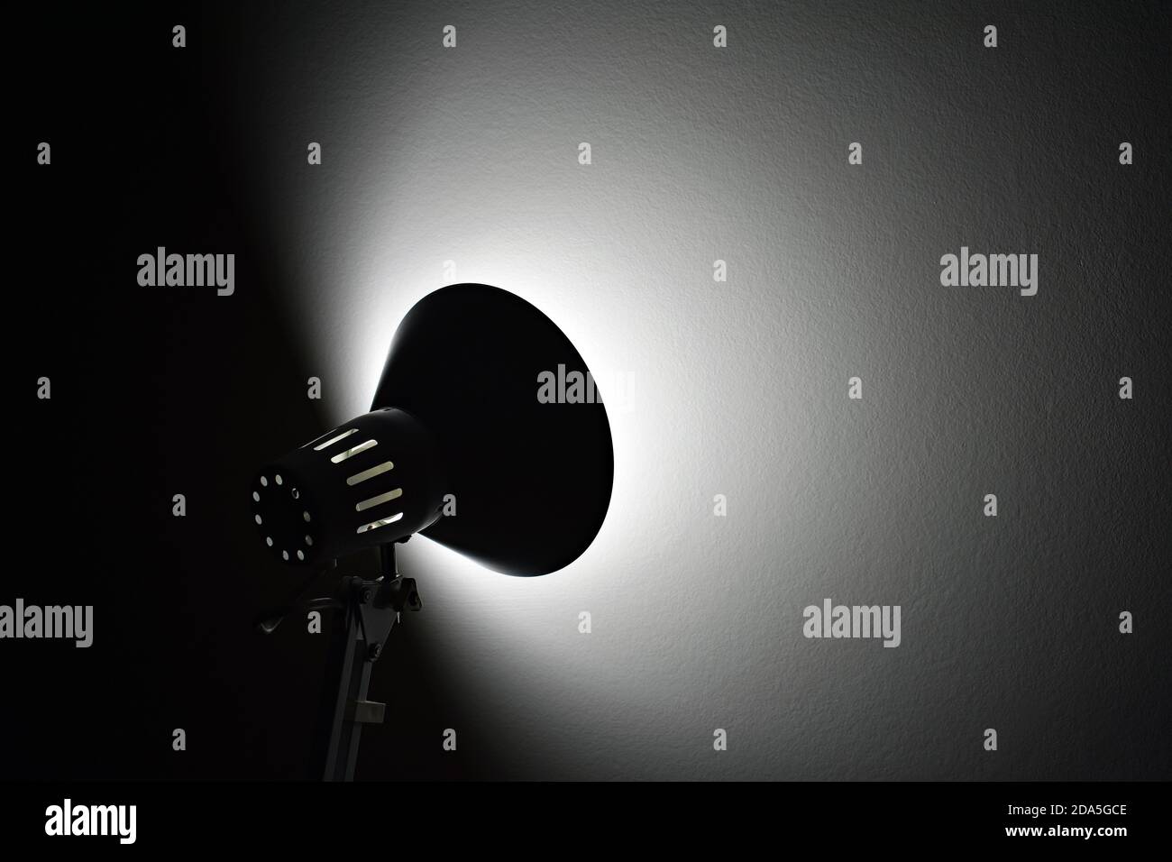 An adjustable desk lamp in shadow throwing a light onto a plain white ...