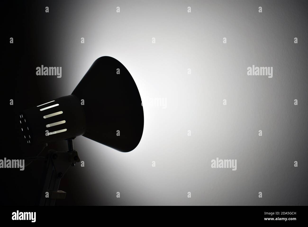 An adjustable desk lamp throwing a spotlight onto a plain white wall ...