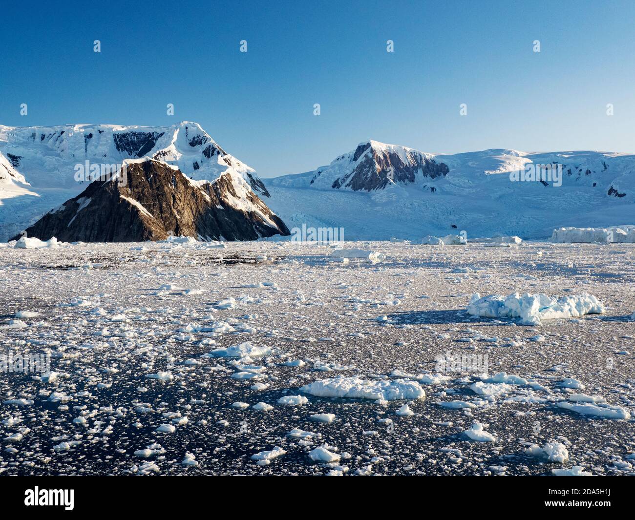 Ice-capped mountains reflected in the brash ice of Neko Harbor ...