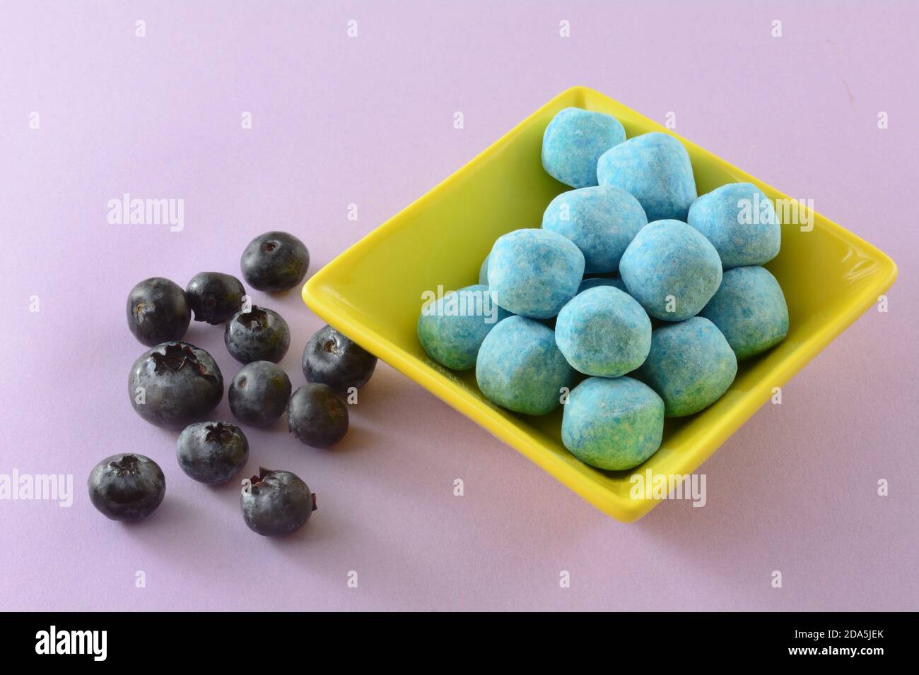 Sour blueberry bonbon candy in yellow candy dish with fresh raw ...