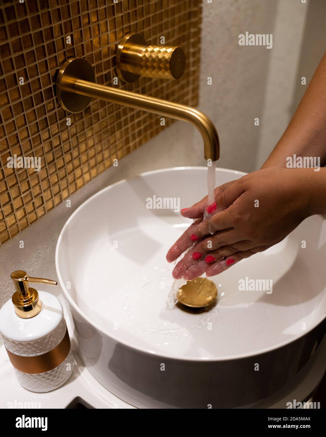 Woman with a red manicure washing hands in luxury interior bath sink ...