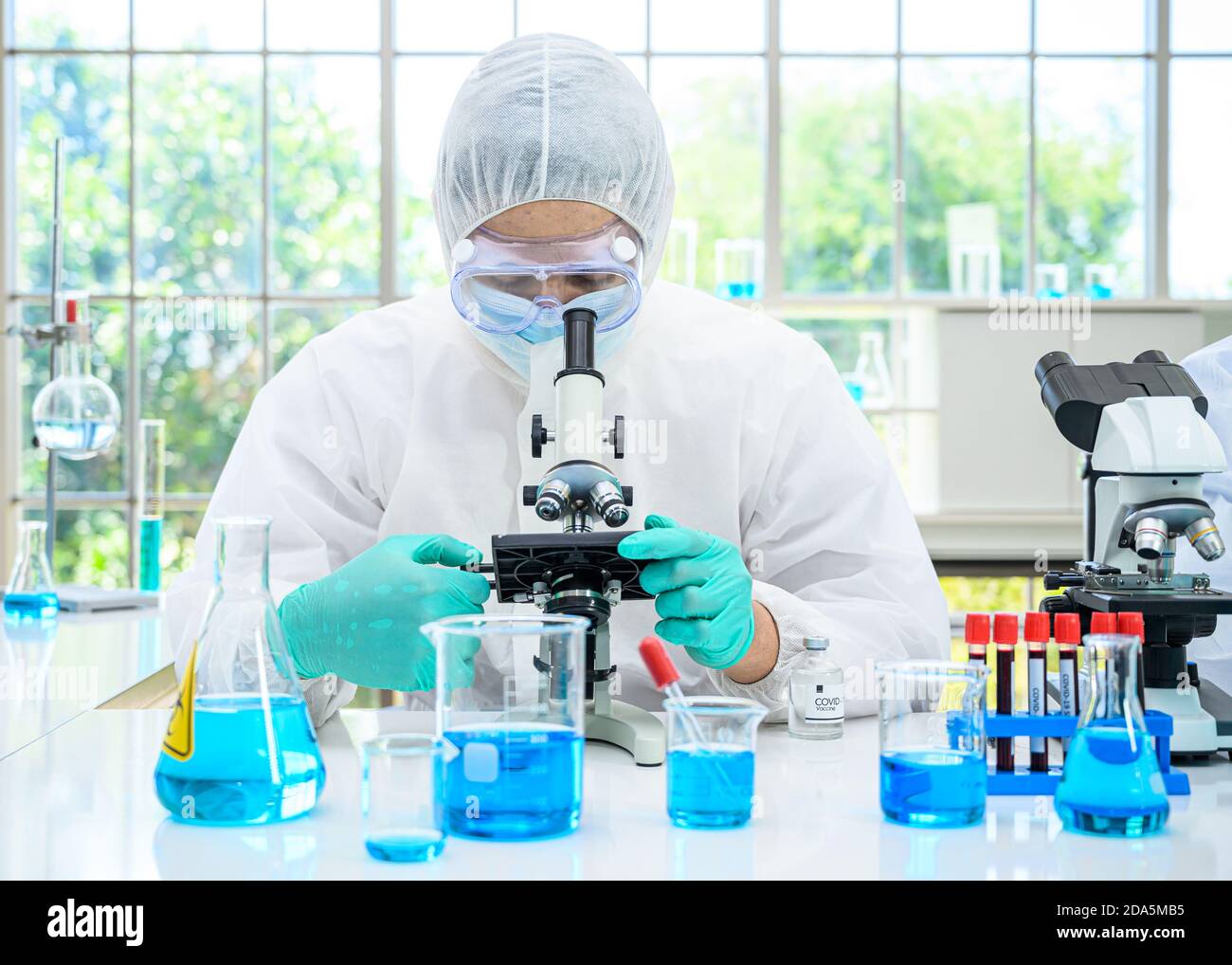 Male scientist wearing protection suit working with Microscope and many ...
