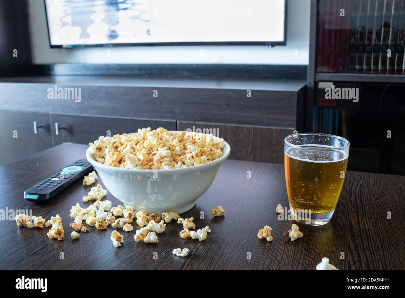 A bowl full of popcorn, some popcorn fallen on the coffee table next to ...