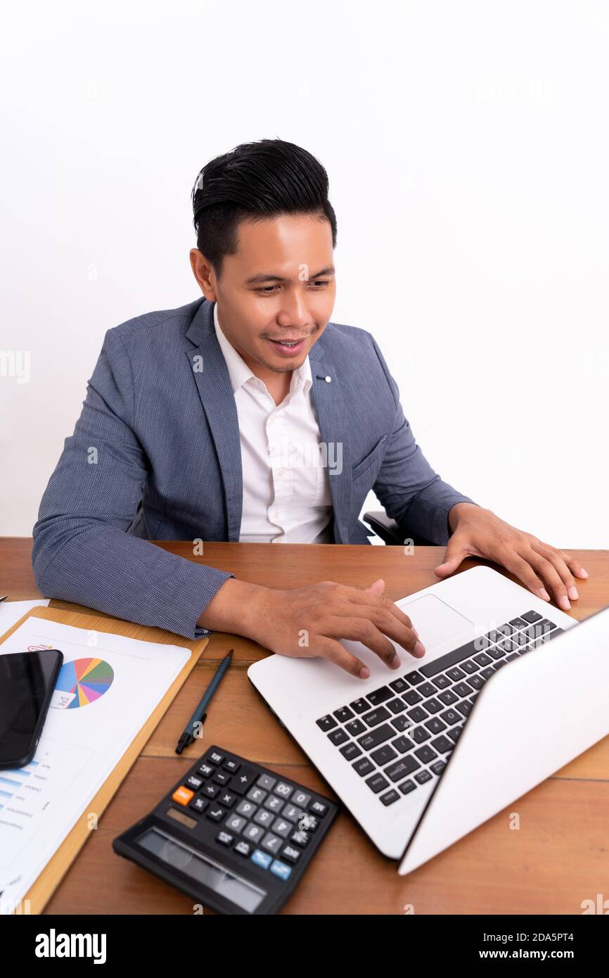 an attractive and cheerful young business man working on a laptop and ...