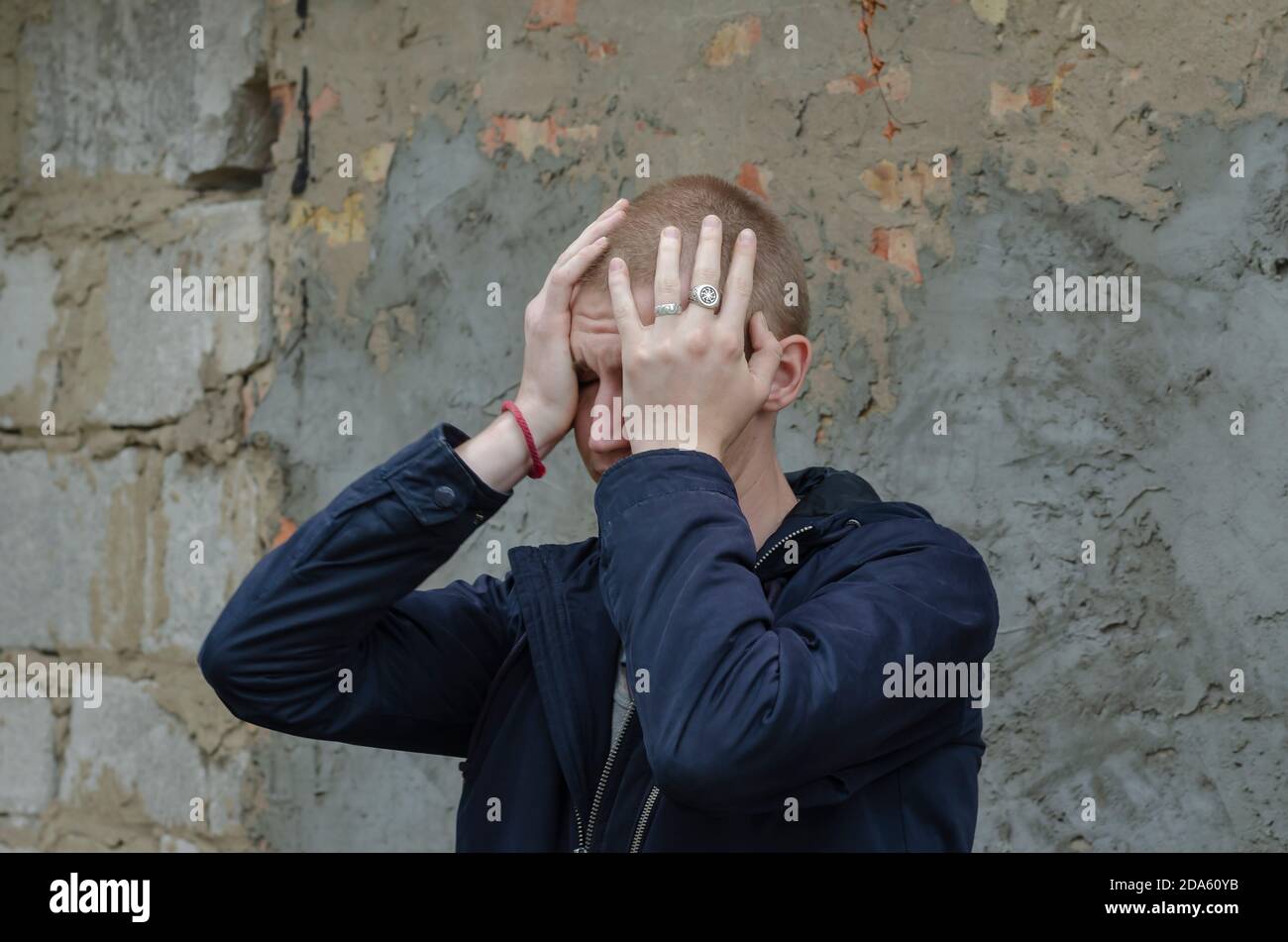 Young man endures grief by the gray concrete wall. Bald Man cries with ...