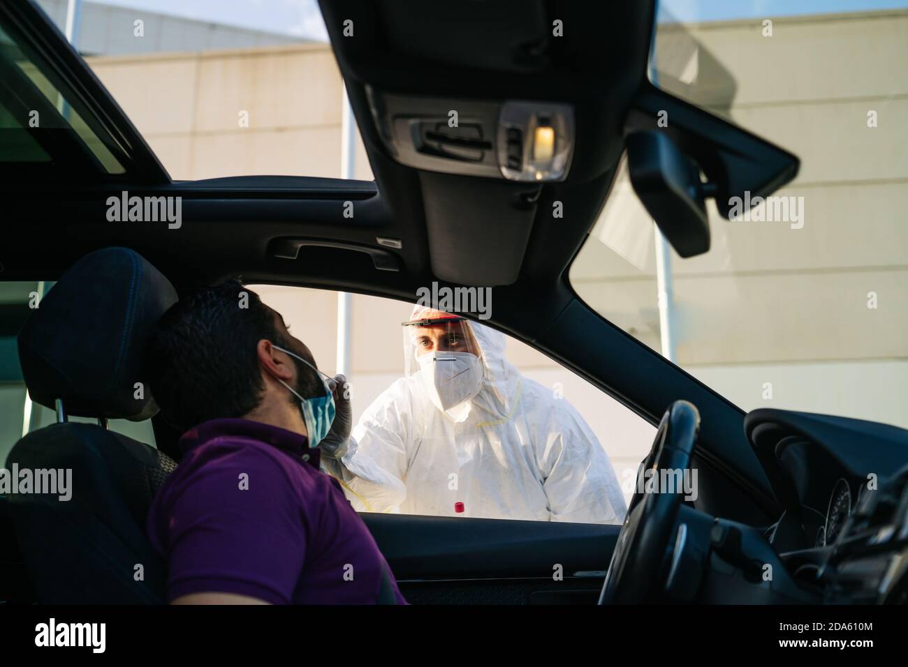 Doctor doing a PCR test COVID-19 on a patient through the car window ...