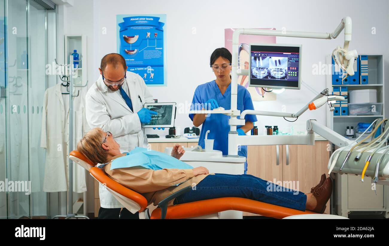 Dentist showing on tablet teeth x-ray reviewing it with patient. Doctor ...