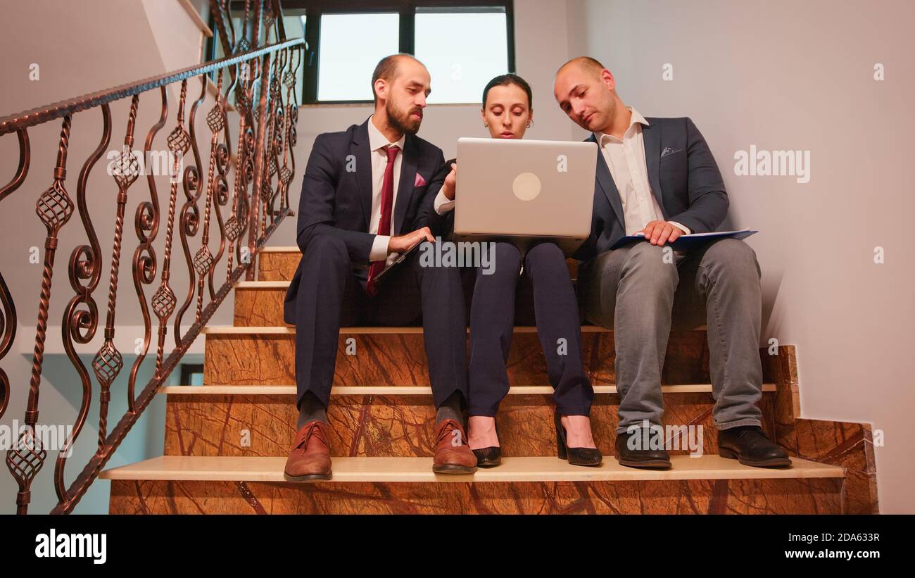 Overworked business colleagues doing overtime sitting on stairs using ...