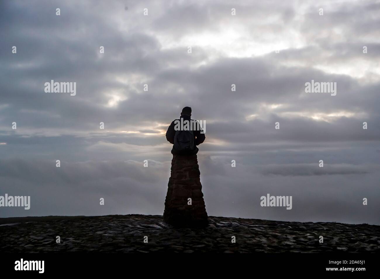 A man sits on a trig point at the top of Mam Tor, near Castleton in the ...