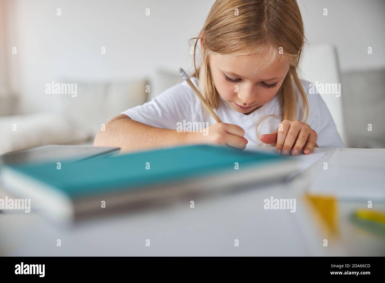 Thoughtful small miss writing letter at the table in room inside Stock ...
