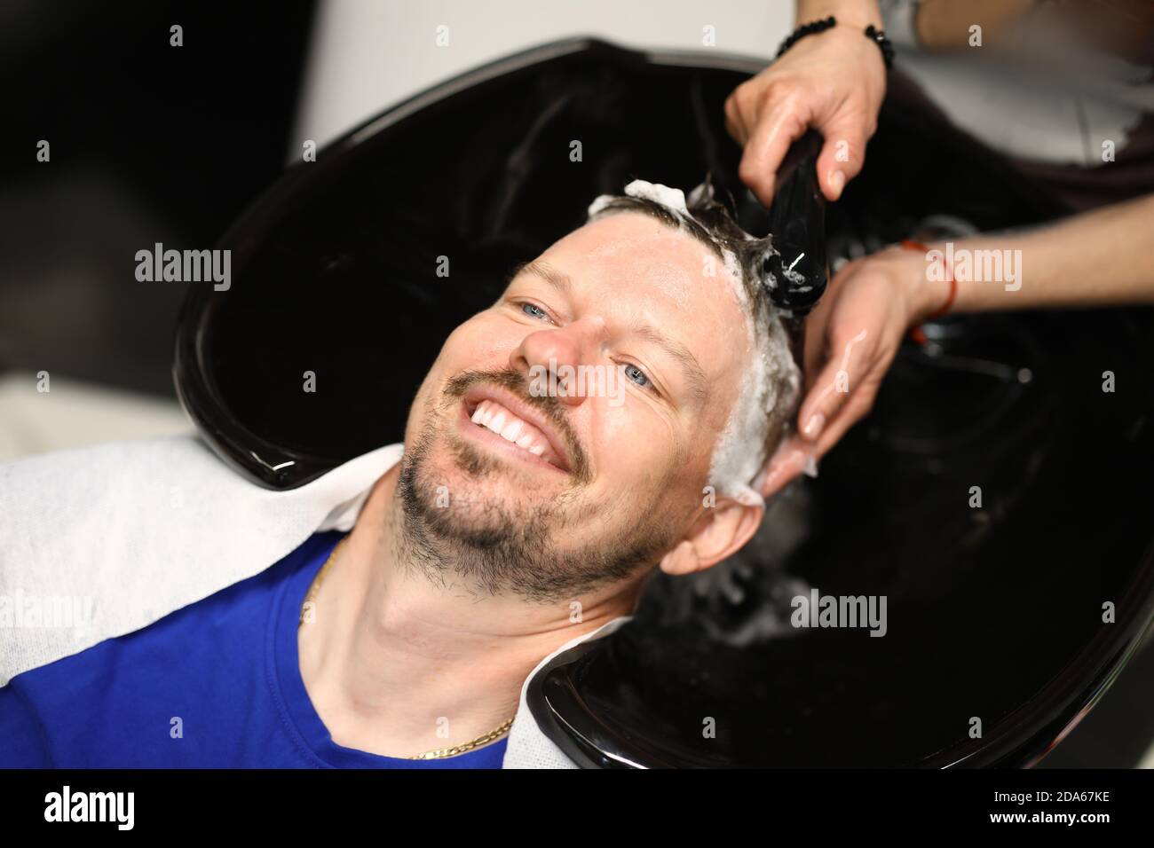 Portrait of smiling man who is being washed with shampoo in salon by ...