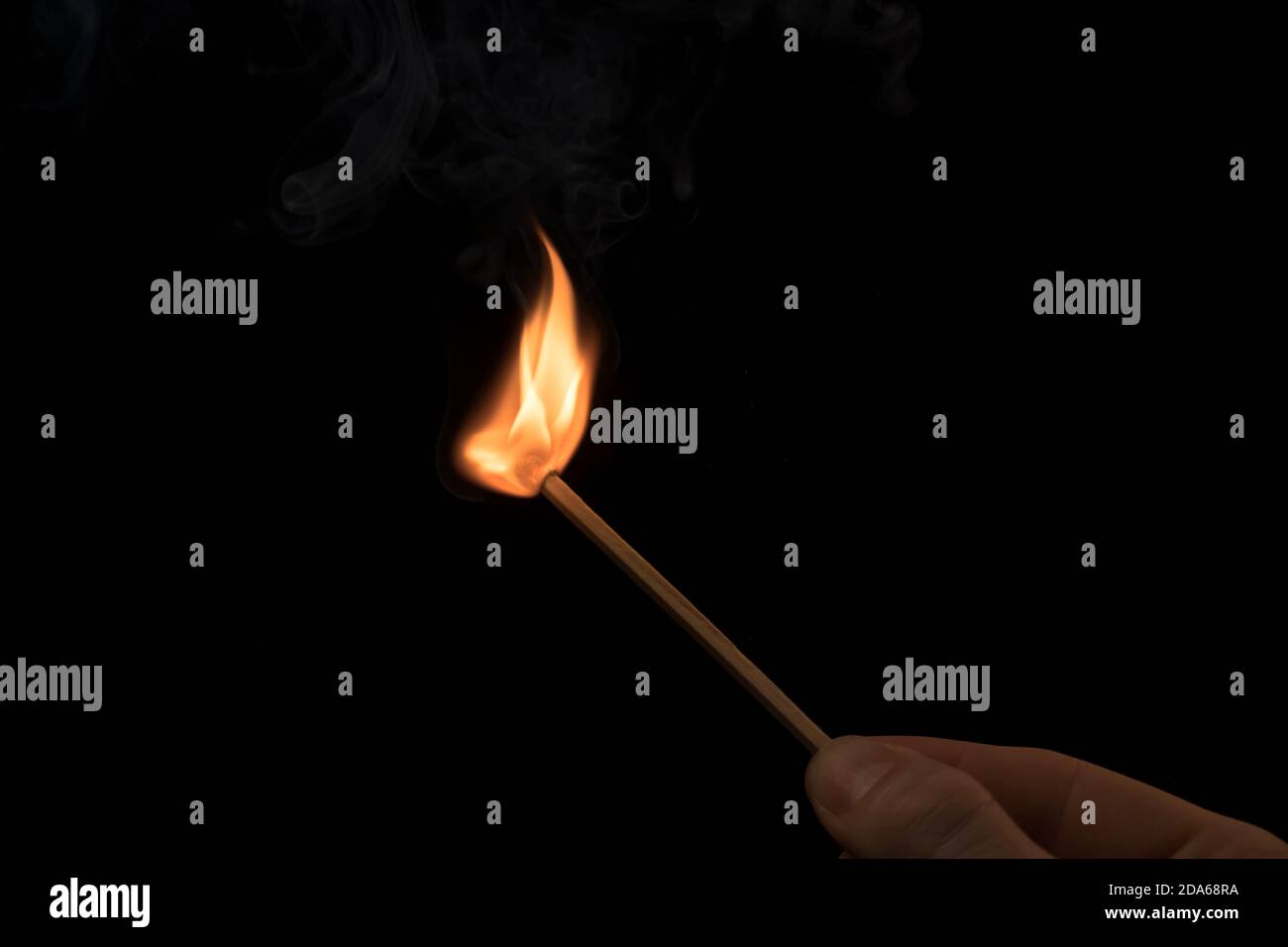 Hand holding a lighted match with fire flame and smoke on a black ...
