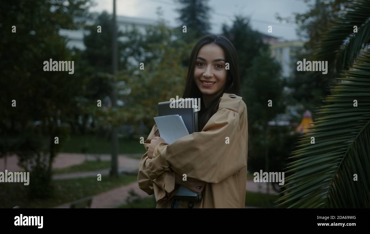 Young, college student woman in coat with laptop and documents in hands ...