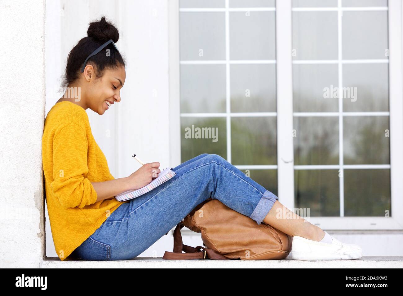 Side view portrait of happy young woman sitting outdoors writing a book ...