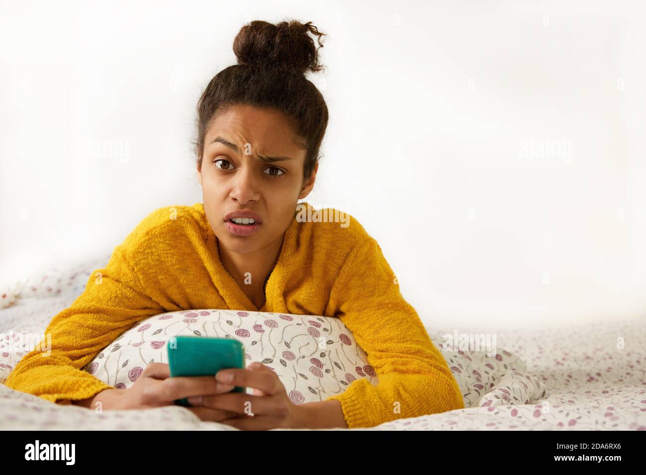 Portrait of a young woman with confused face expression sitting in bed ...