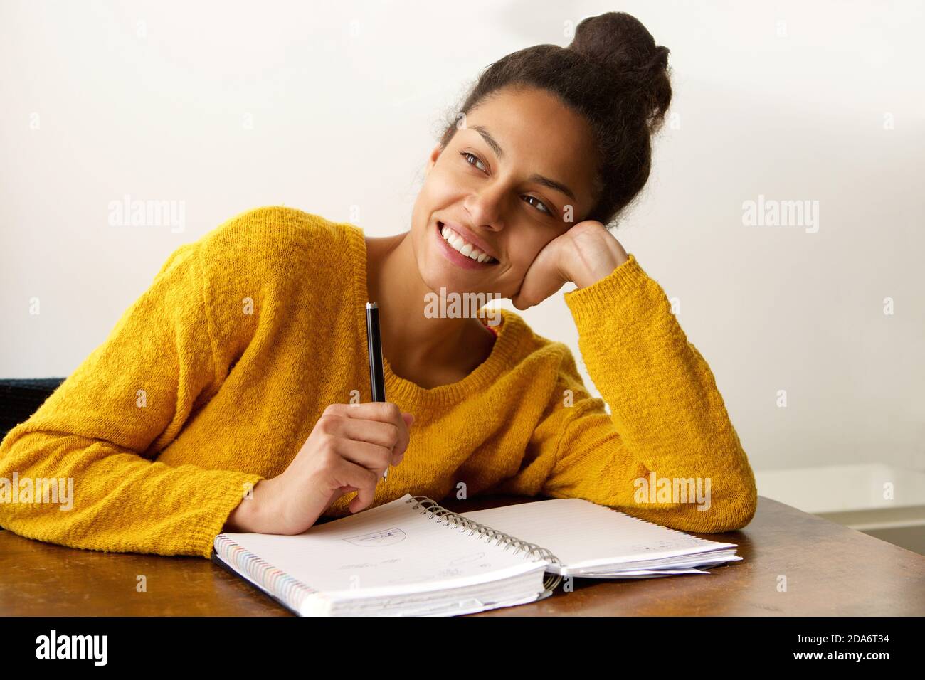 Portrait of a smiling female student thinking with with pen and paper ...