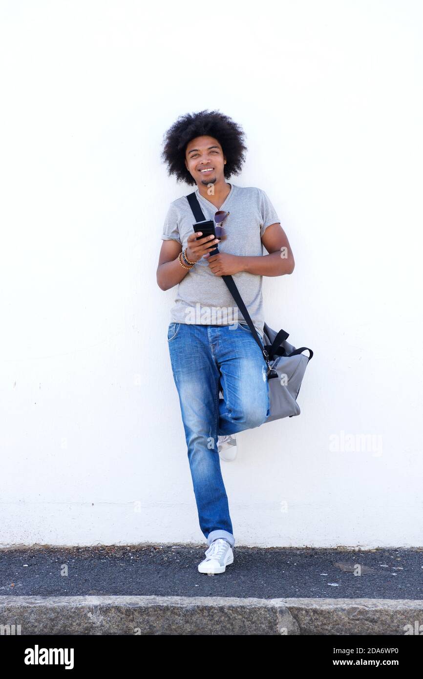 Full length portrait of a cool guy standing outside with cell phone and ...