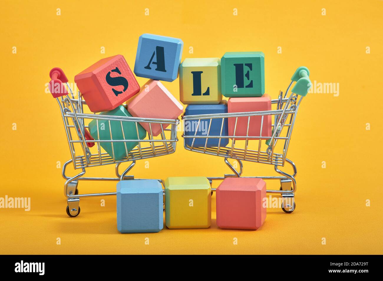 A miniature shopping cart and multi-colored cubes on yellow background ...
