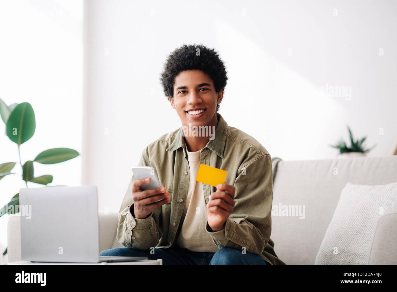 Happy black teen guy with laptop computer using cellphone and credit ...