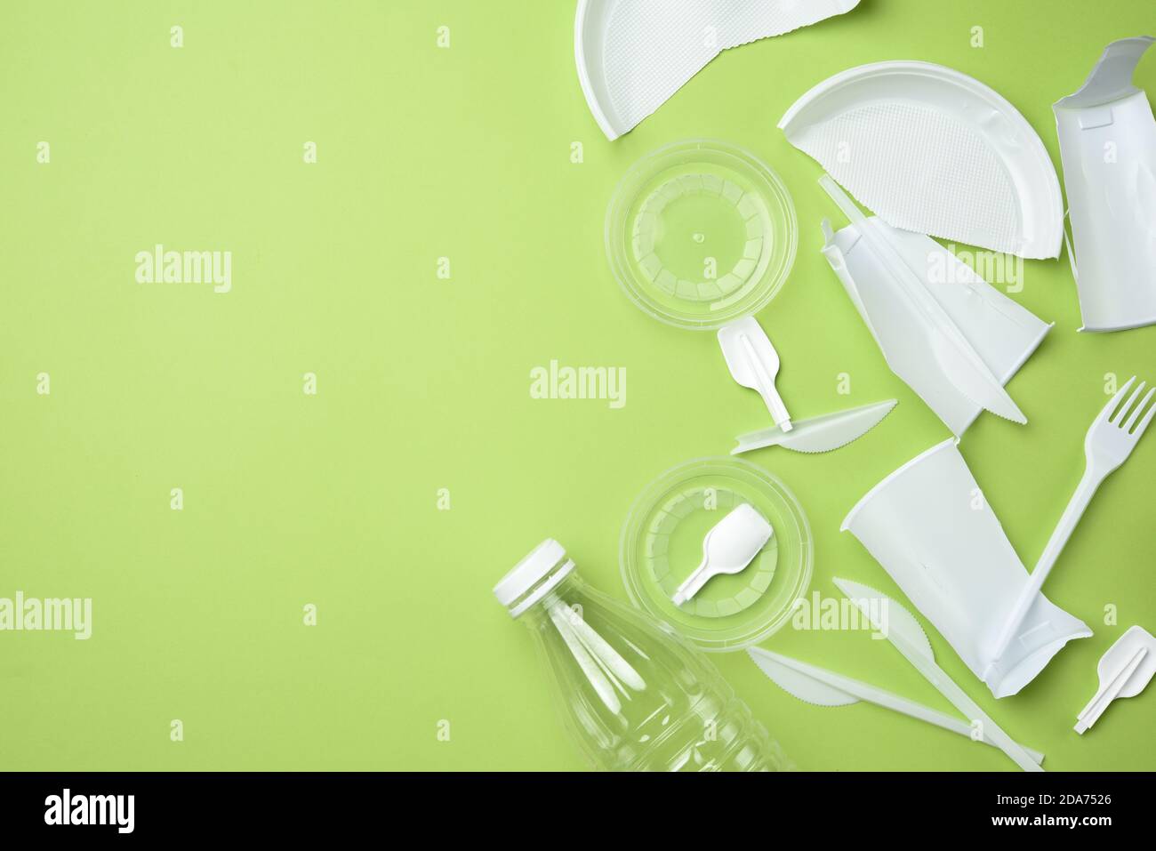 broken white plastic tableware, transparent bottle on green background ...
