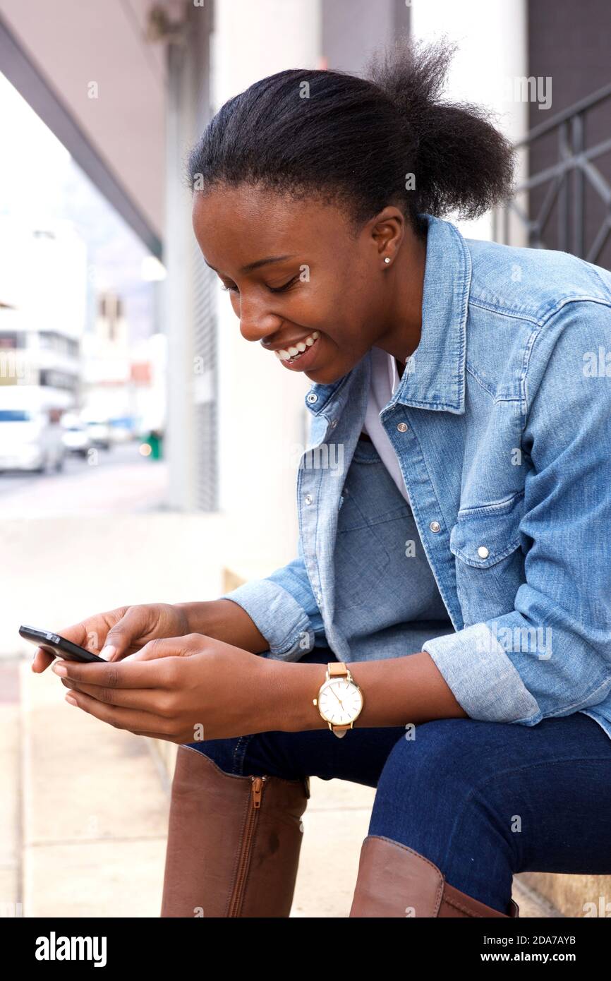 Side portrait of happy african woman sitting outside texting her ...