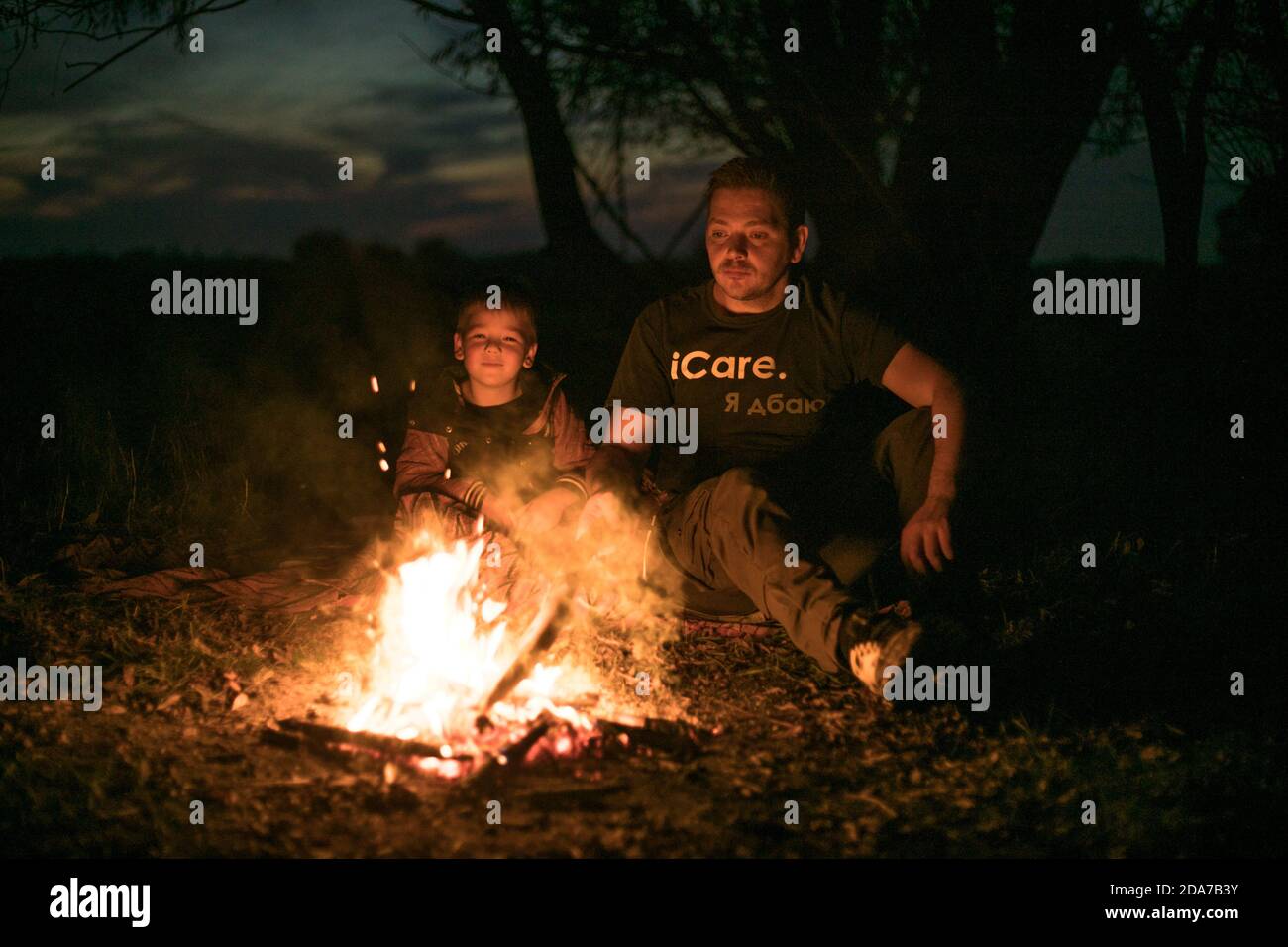 Father and little cute son sitting by the fire in the forest. Best ...