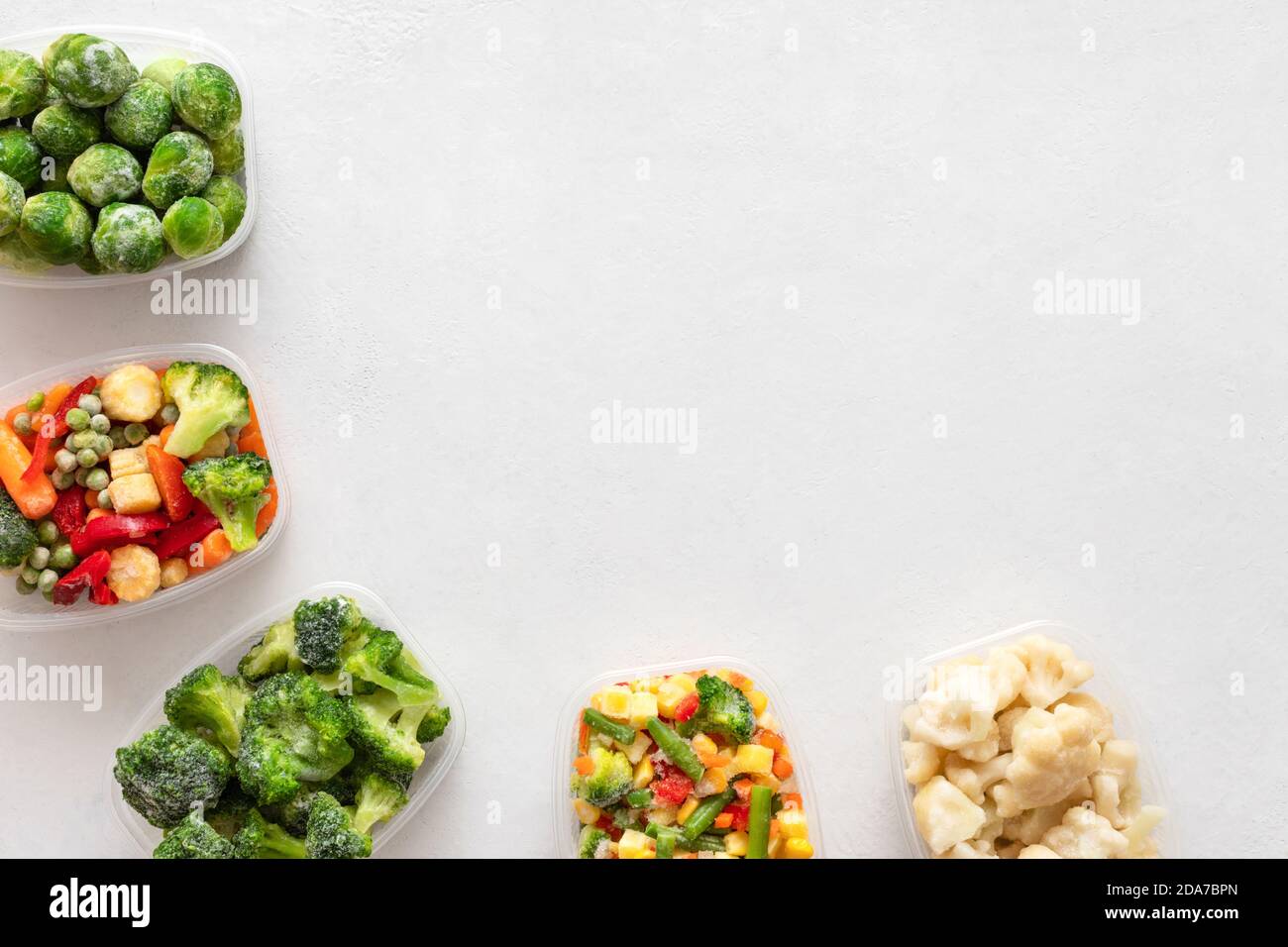 Frozen colorful vegetables in containers on a white background. Copy ...