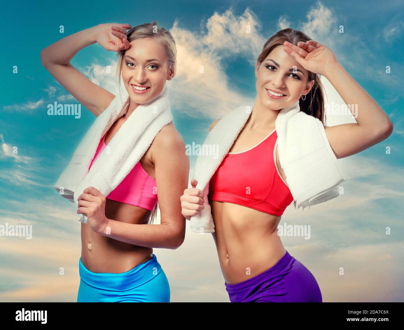 Two beautiful girls after workout with towels posing on cloudy sky background. Wellness, sporty ...