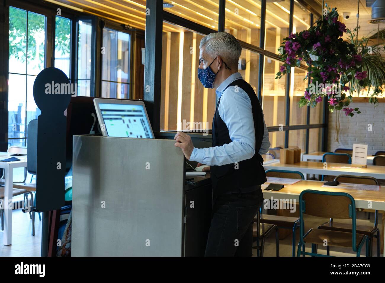 Waiter wearing face mask checking the tables on a counter touch screen ...