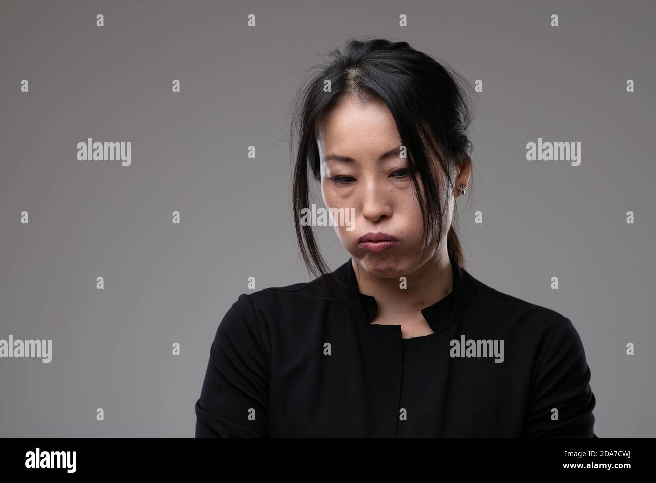 Petulant sulky Asian woman pouting her lips and looking down with a ...