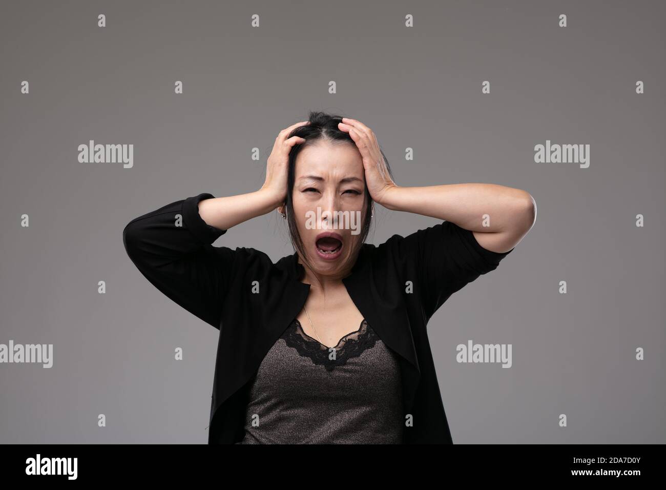 Sorrowful grieving Asian woman wailing in anguish holding her hands to ...